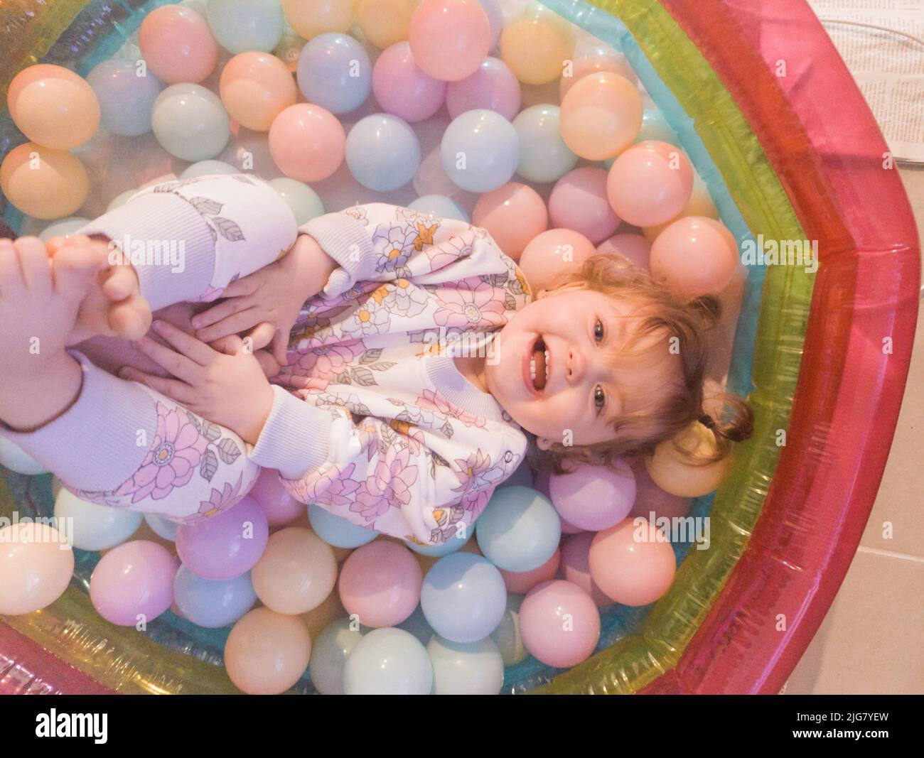 A top view of a cute Australian baby girl in a pool full of colorful ...