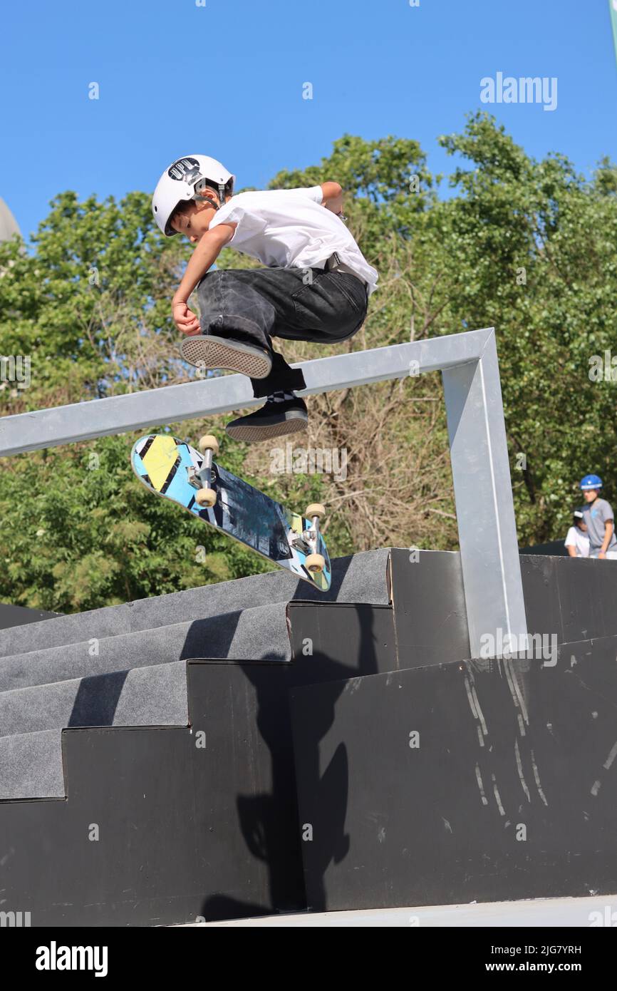 A little boy makes a jump on skateboard on springboard with a blue sky ...