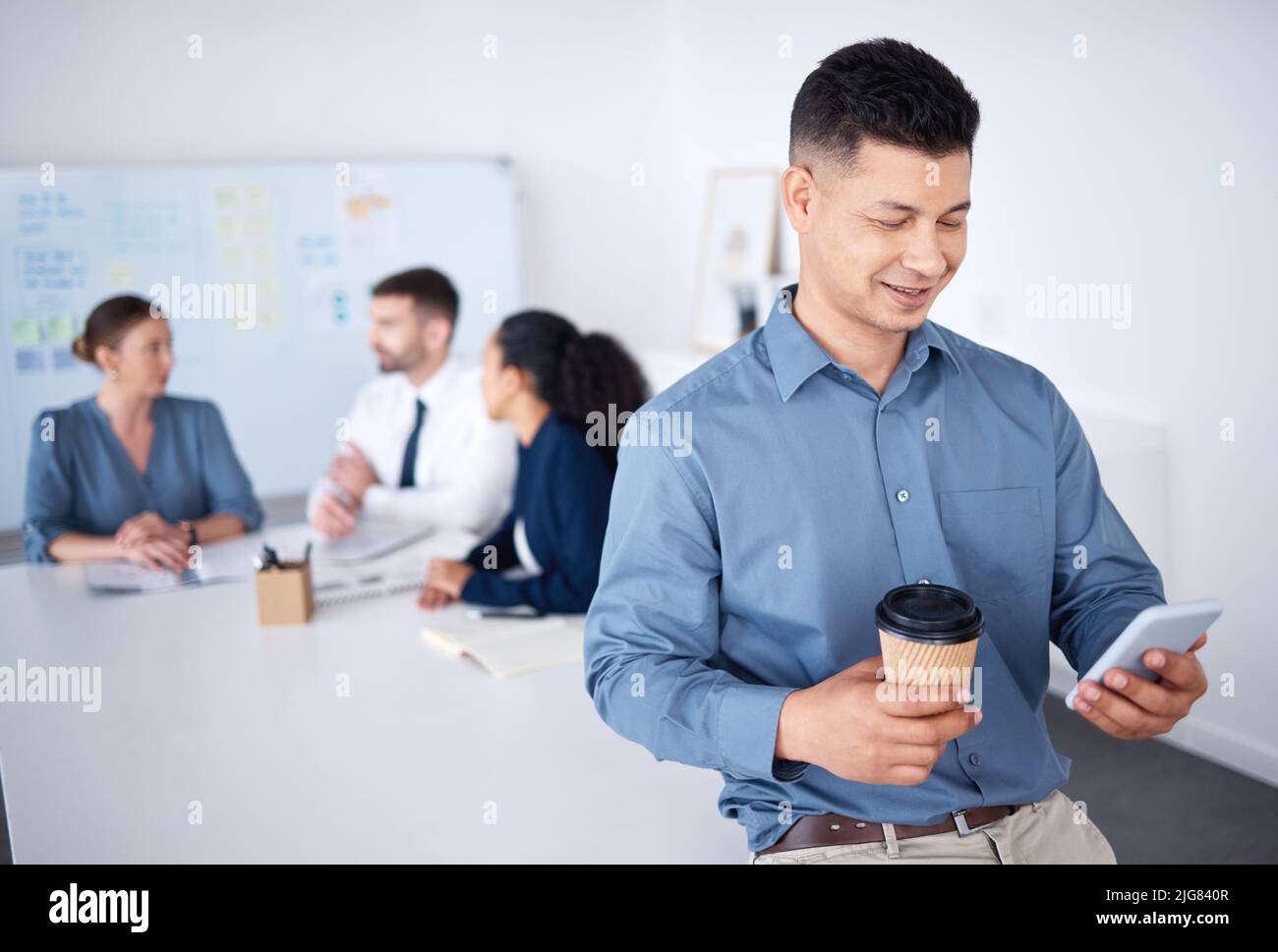 Smiling confident mixed race businessman in boardroom using cellphone ...