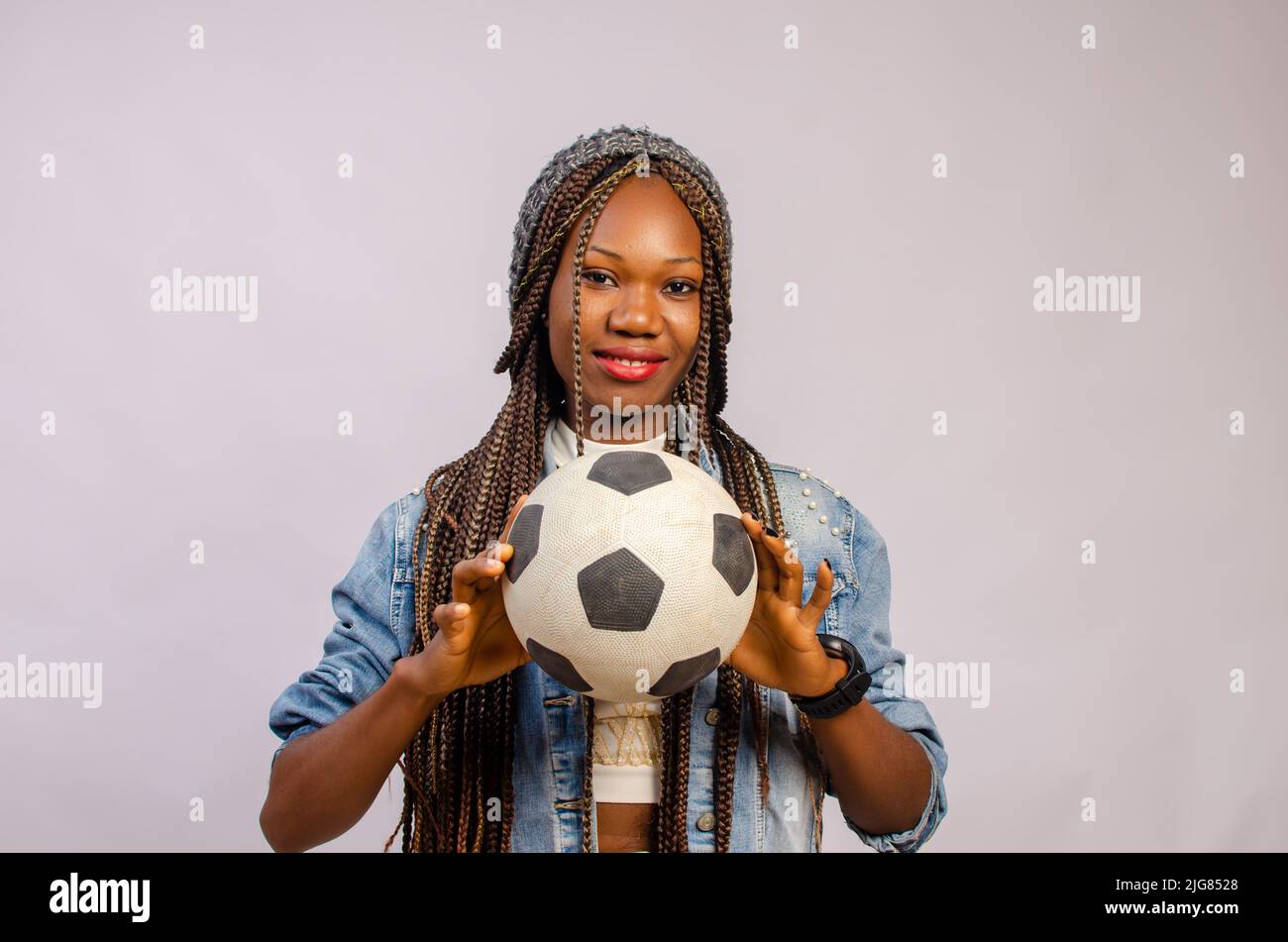 The young African confident lady holding football ball isolated on pale ...