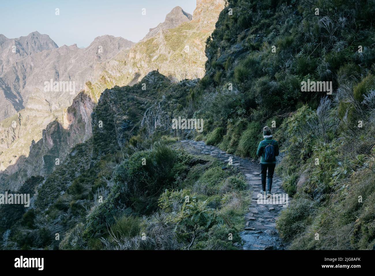 A back view of a woman with backpack walking on narrow mountain path in ...