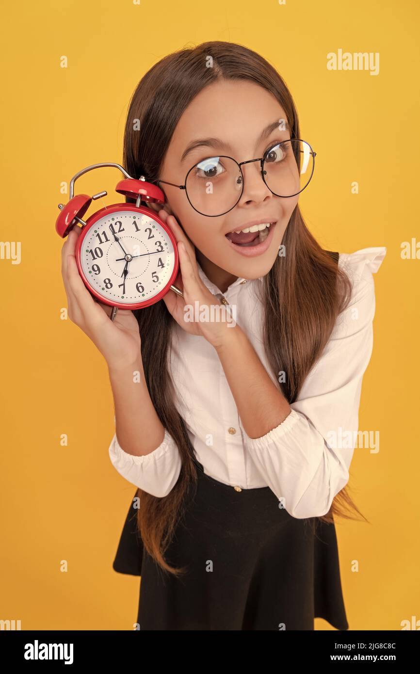 amazed child in school uniform and glasses listen alarm clock ringing ...