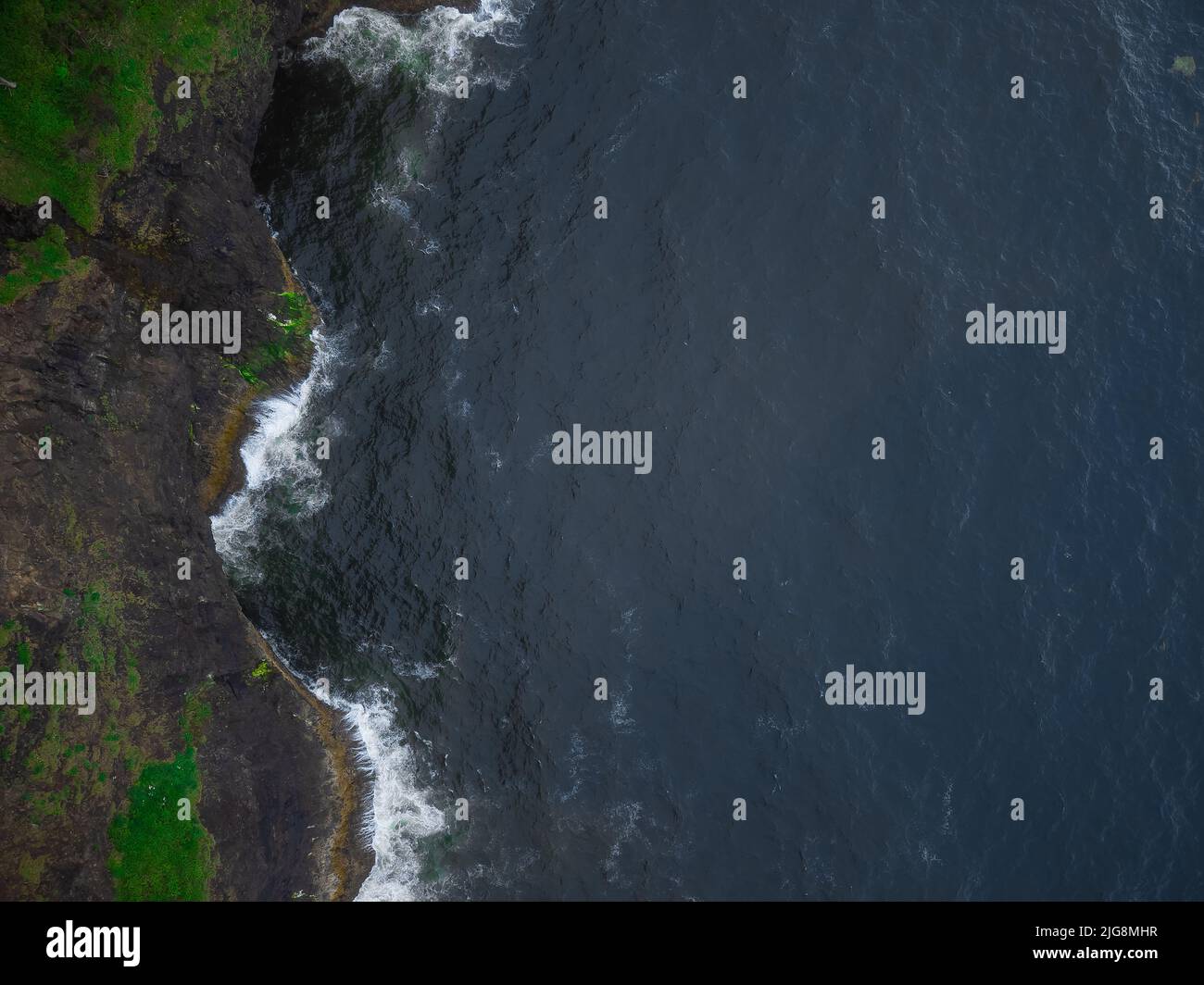Shot from the air. A blue ocean with white foamy waves beats against a ...