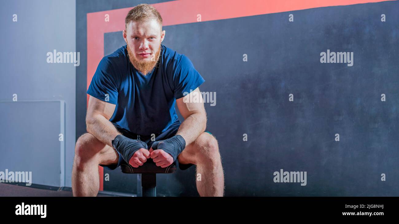 Strong muscular mixed martial arts fighter sits on couch. His hands are ...