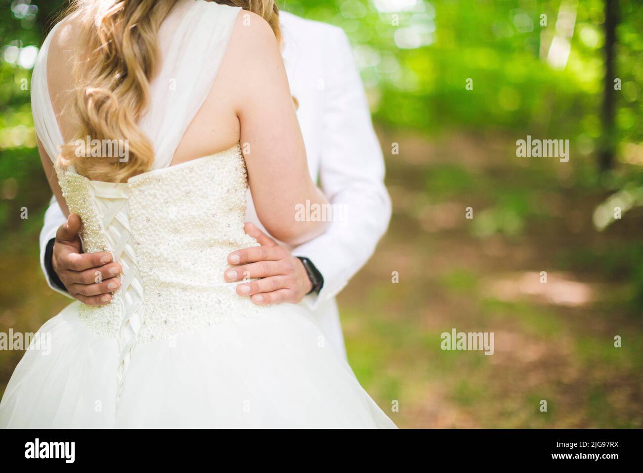 A back view of the bride and the groom in white hugging in the green ...