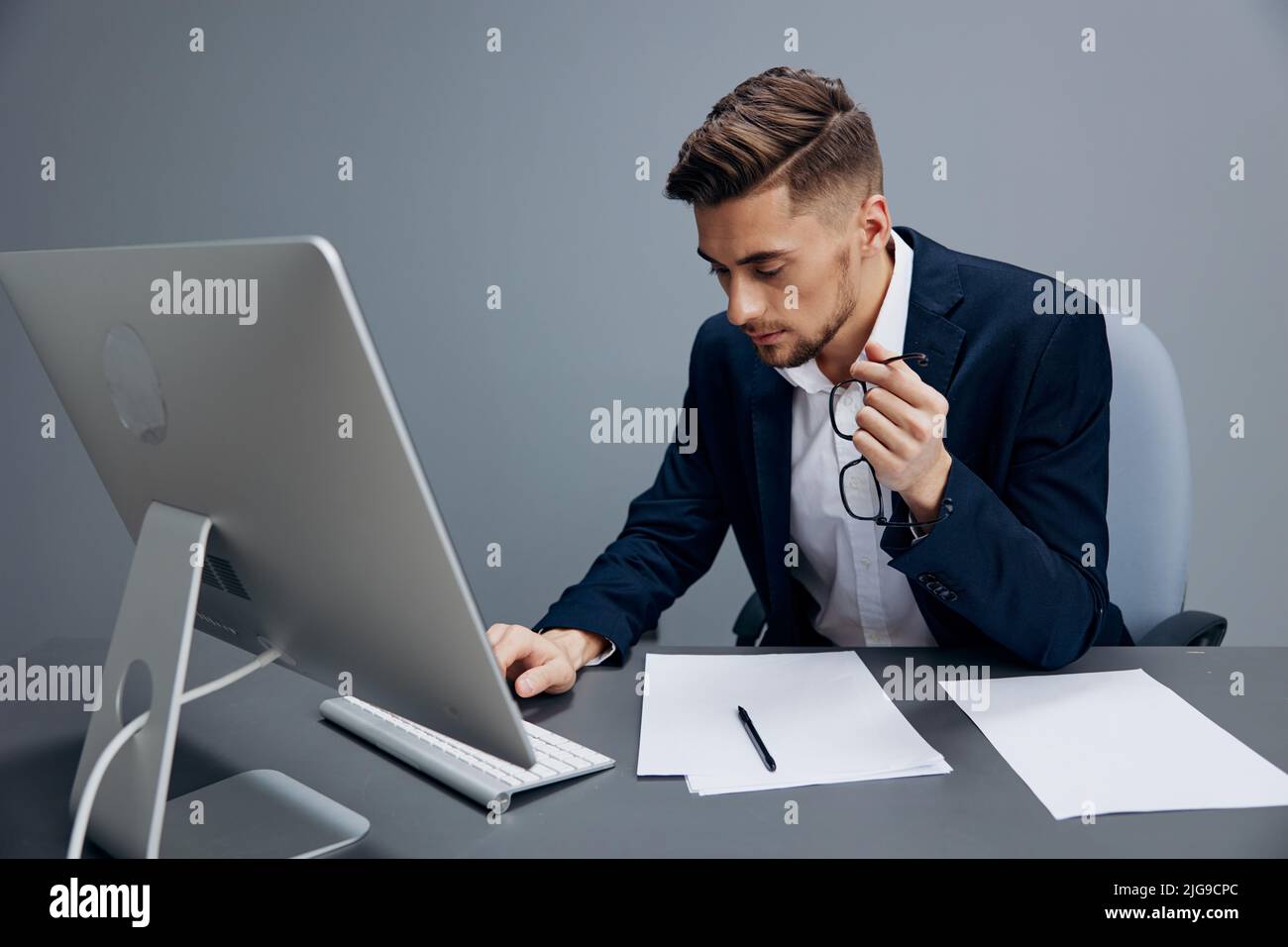 a man in a suit sitting at a desk in front of a computer Gray ...