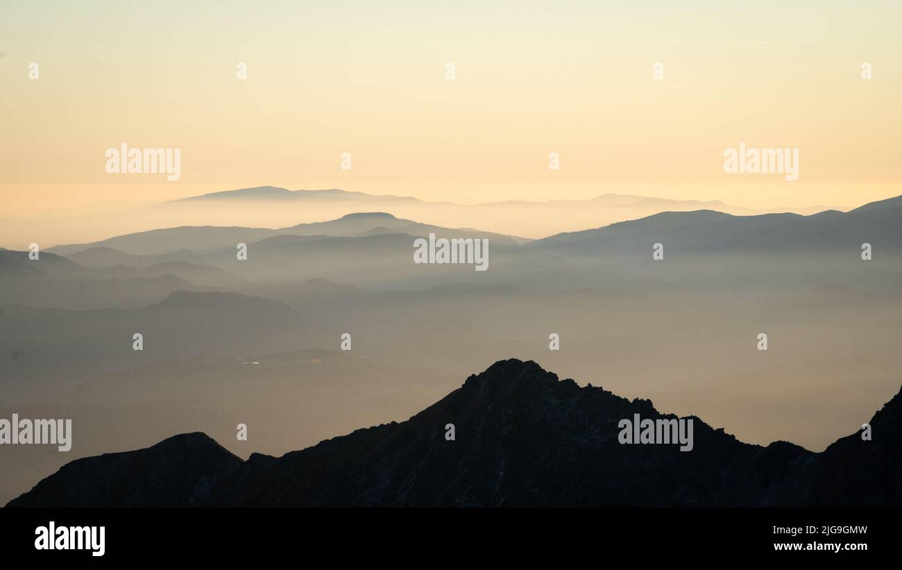 Alpine landscape with mountain ranges silhouettes during foggy sunset ...