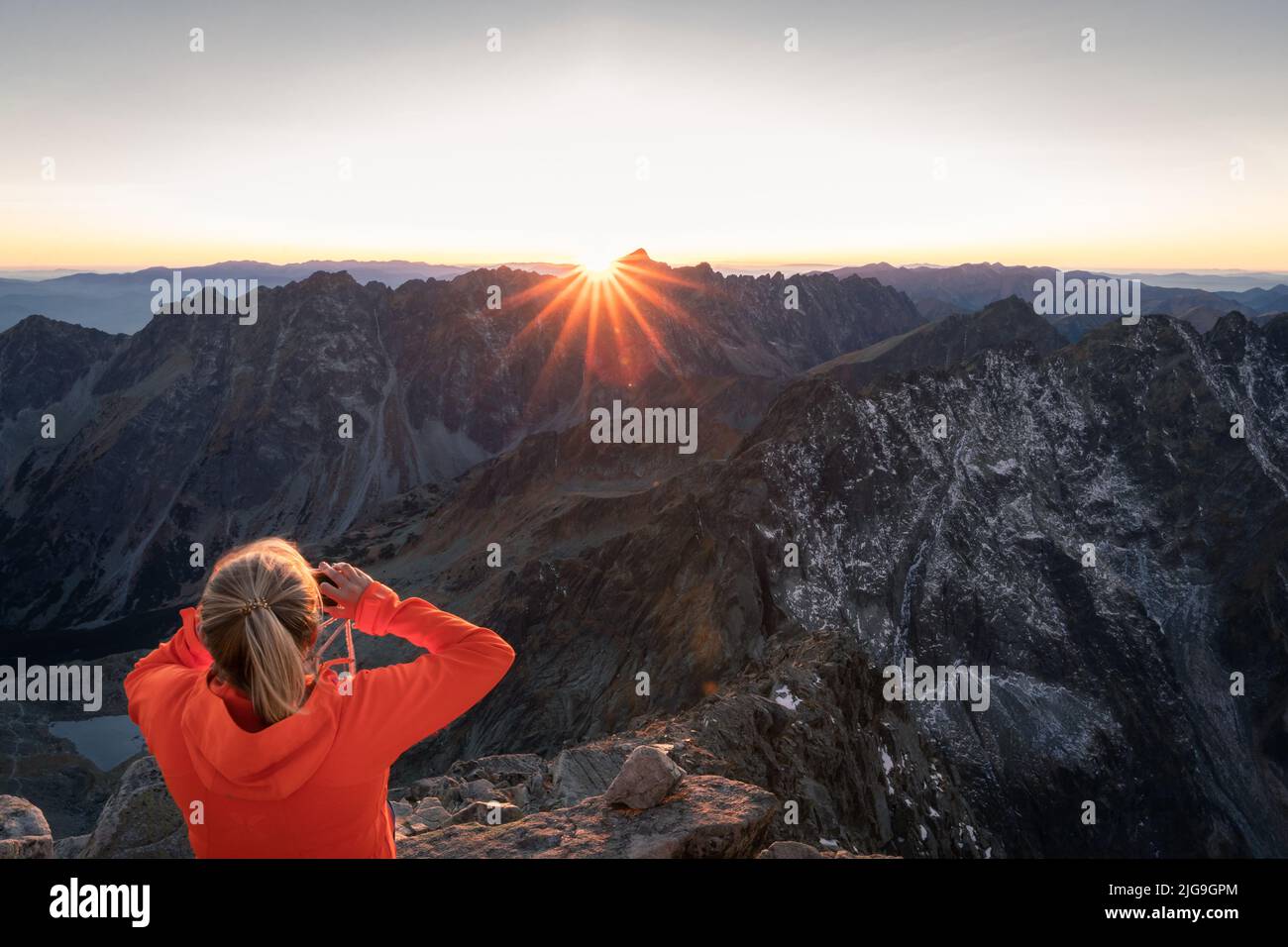 Woman photographing sunset in alpine environment surrounded by rocky ...