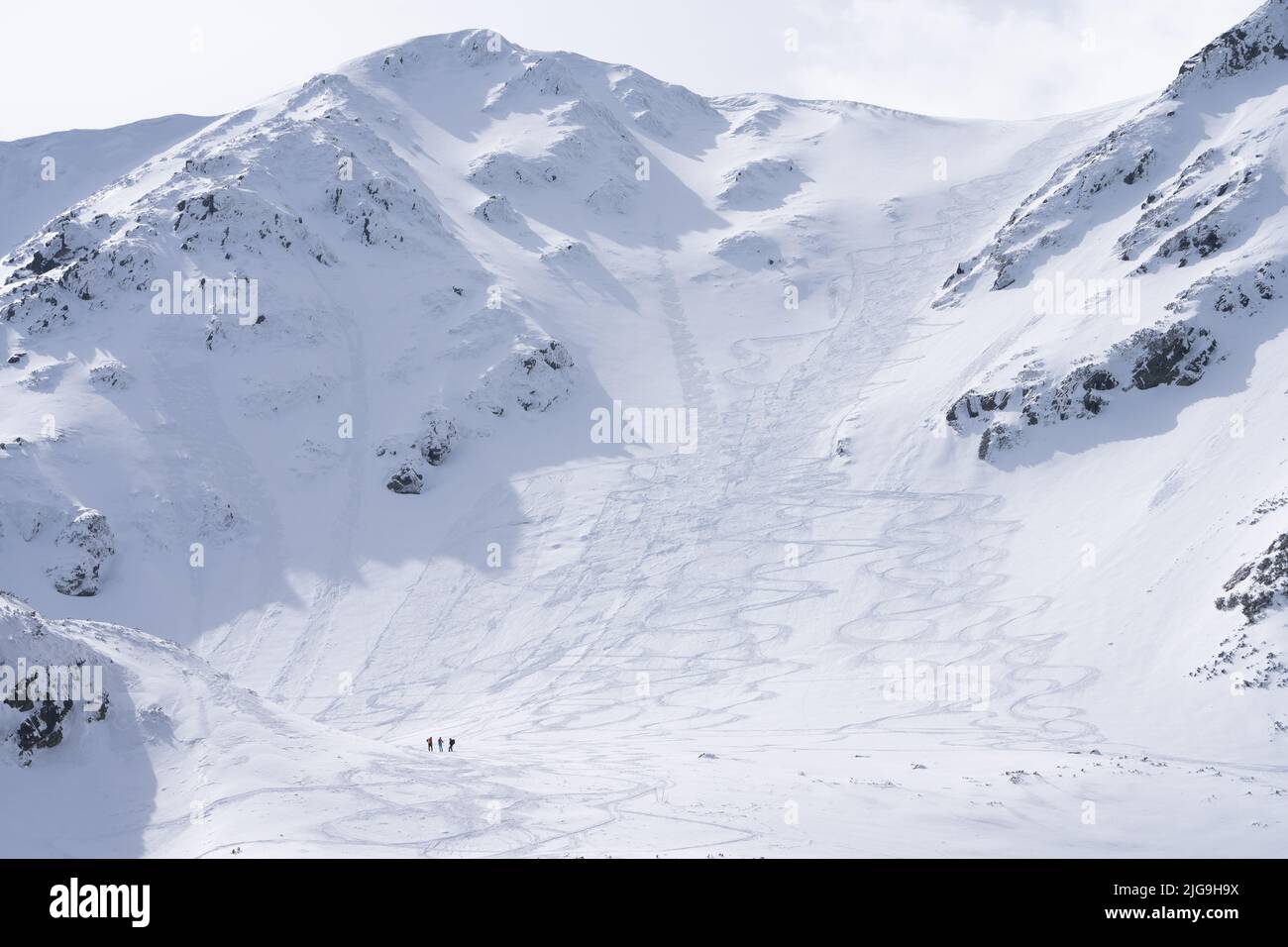Three hikers during winter standing at the bottom of snowy mountain ...