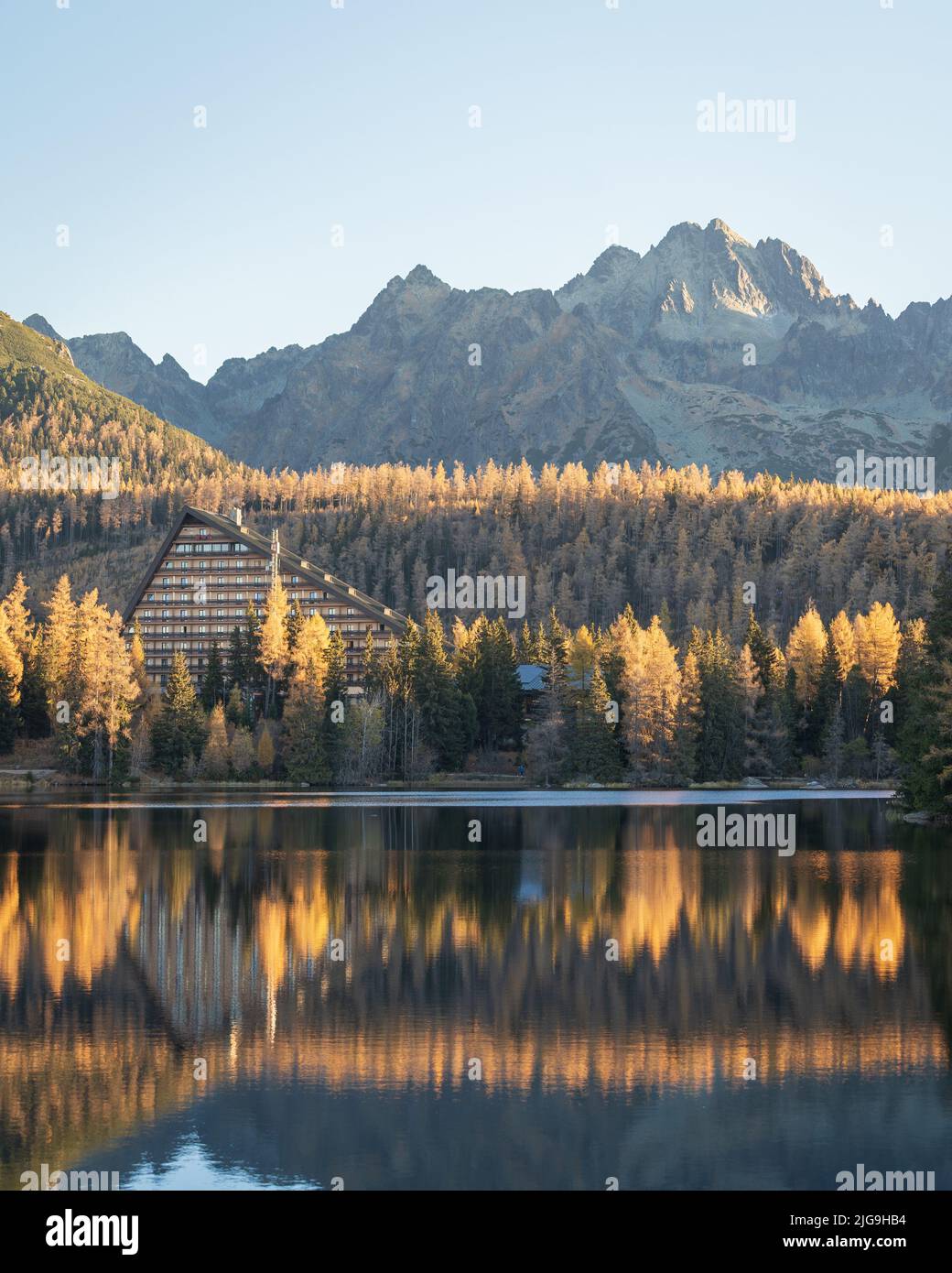 Autumn coloured landscape with a hotel on a bank of a lake with rocky ...