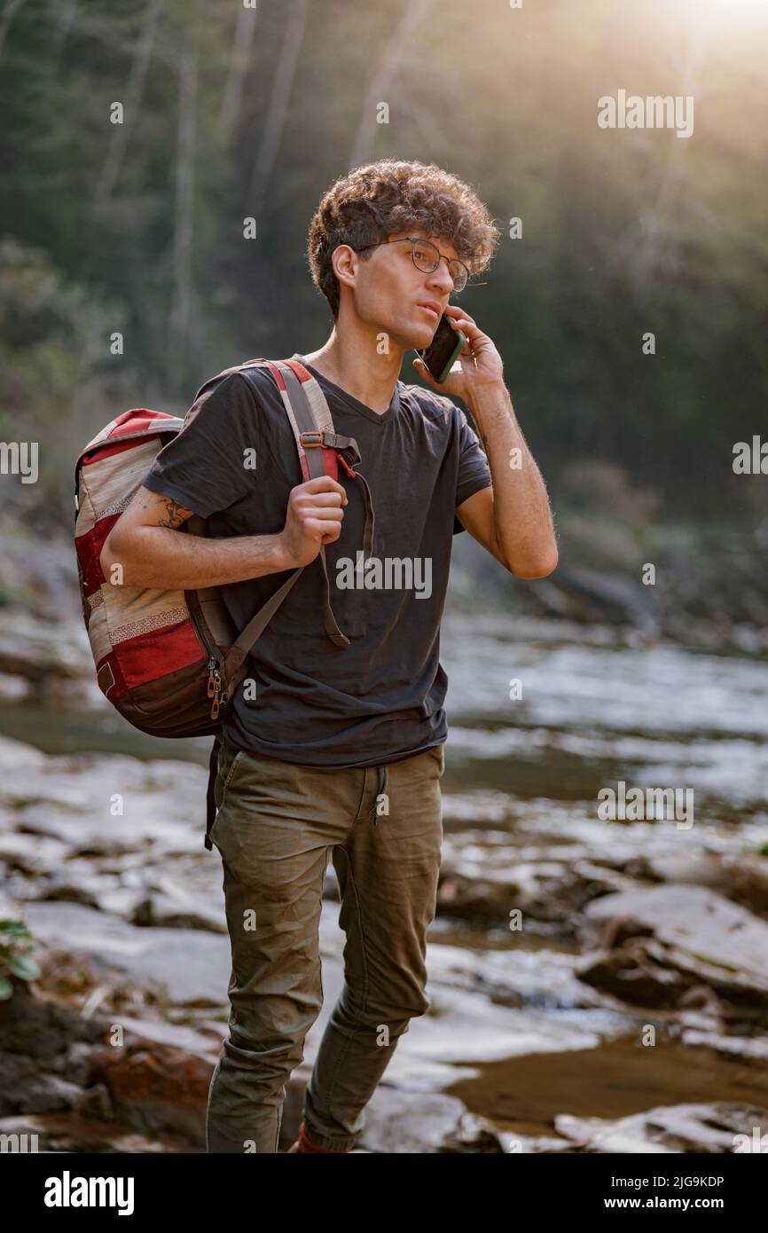 Lost young man tourist with backpack roaming at river in mountains and ...