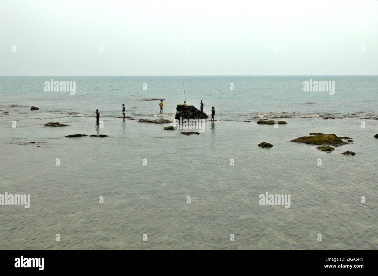 People fishing as they are standing on shallow water on rocky, flat ...