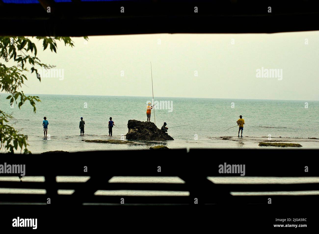 People fishing as they are standing on shallow water on rocky beach ...