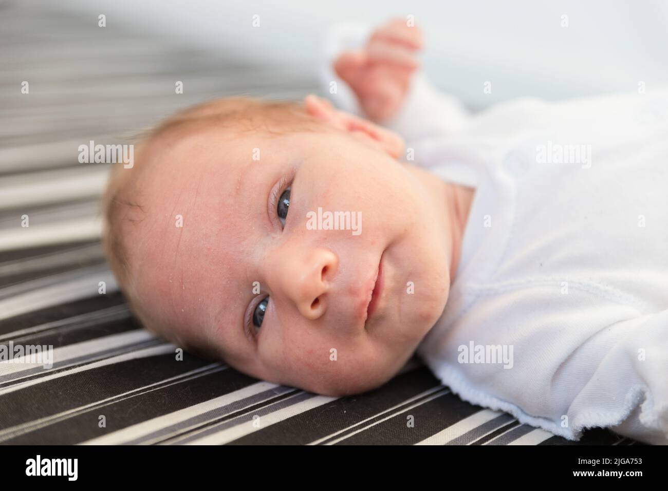 Face of a little baby lying on his back on striped sheet Stock Photo ...