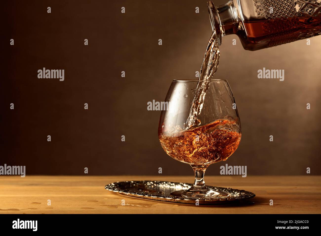Brandy is poured from a decanter into a snifter glass. Cognac on an oak ...