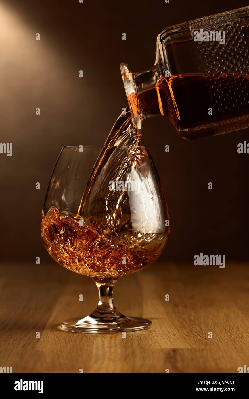 Brandy is poured from a decanter into a snifter glass. Cognac on an oak table Stock Photo - Alamy