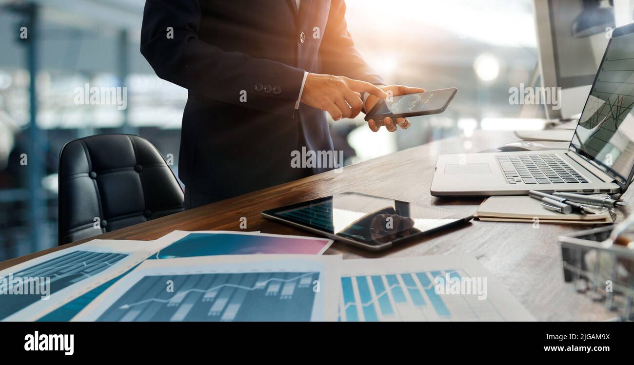 A businessman using mobile smartphone and laptop analyzing sales data ...