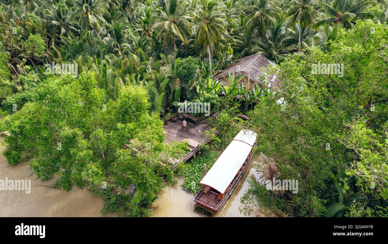 man standing on dock with boat on tropical coastline of Ben Tre along ...