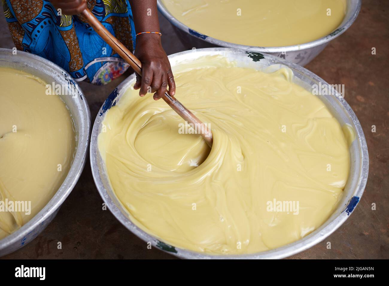 A top view of a black woman making butter in huge bowls with a wooden ...