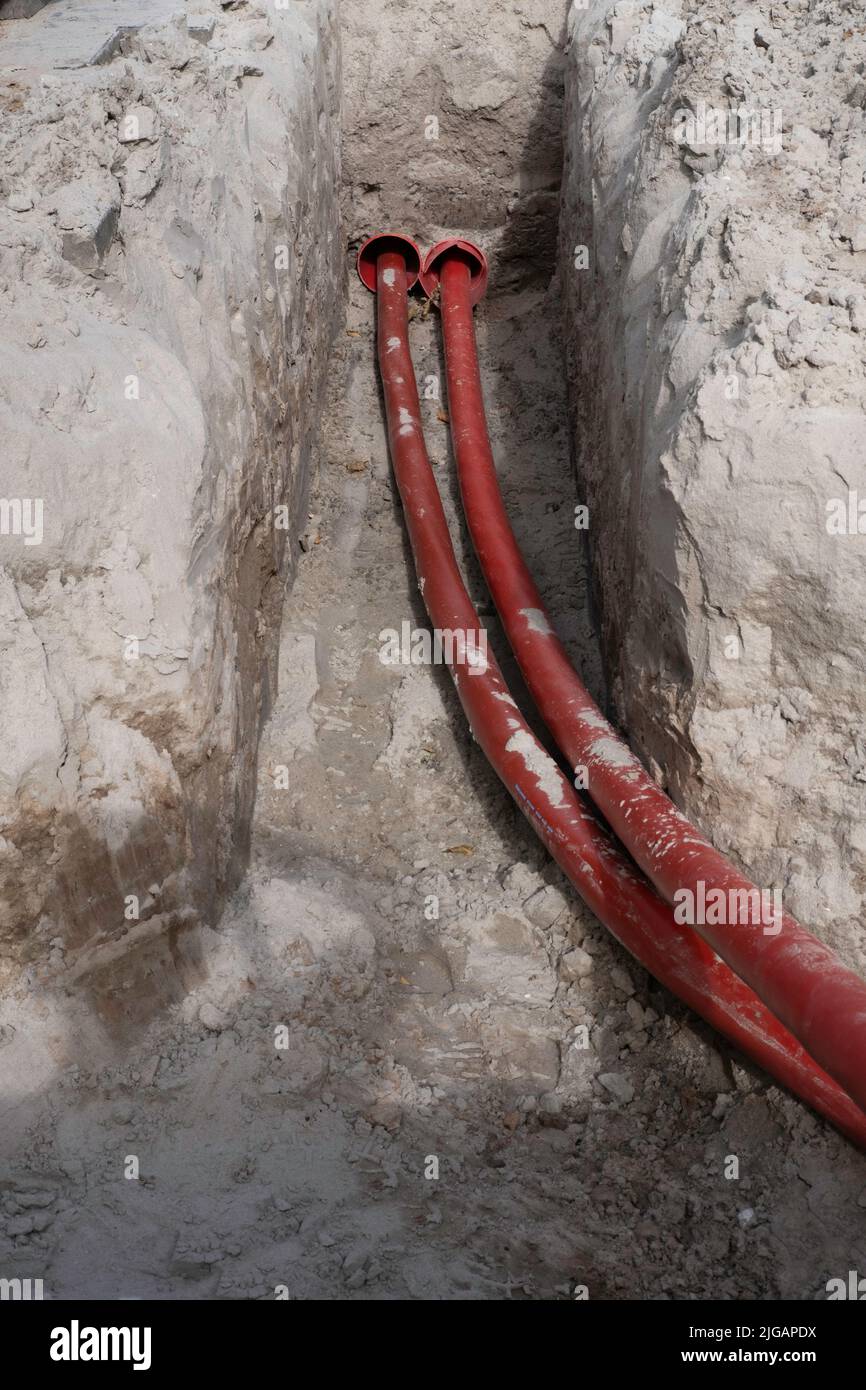 Thick red electricity cables lie in a dug trench in the ground in a ...