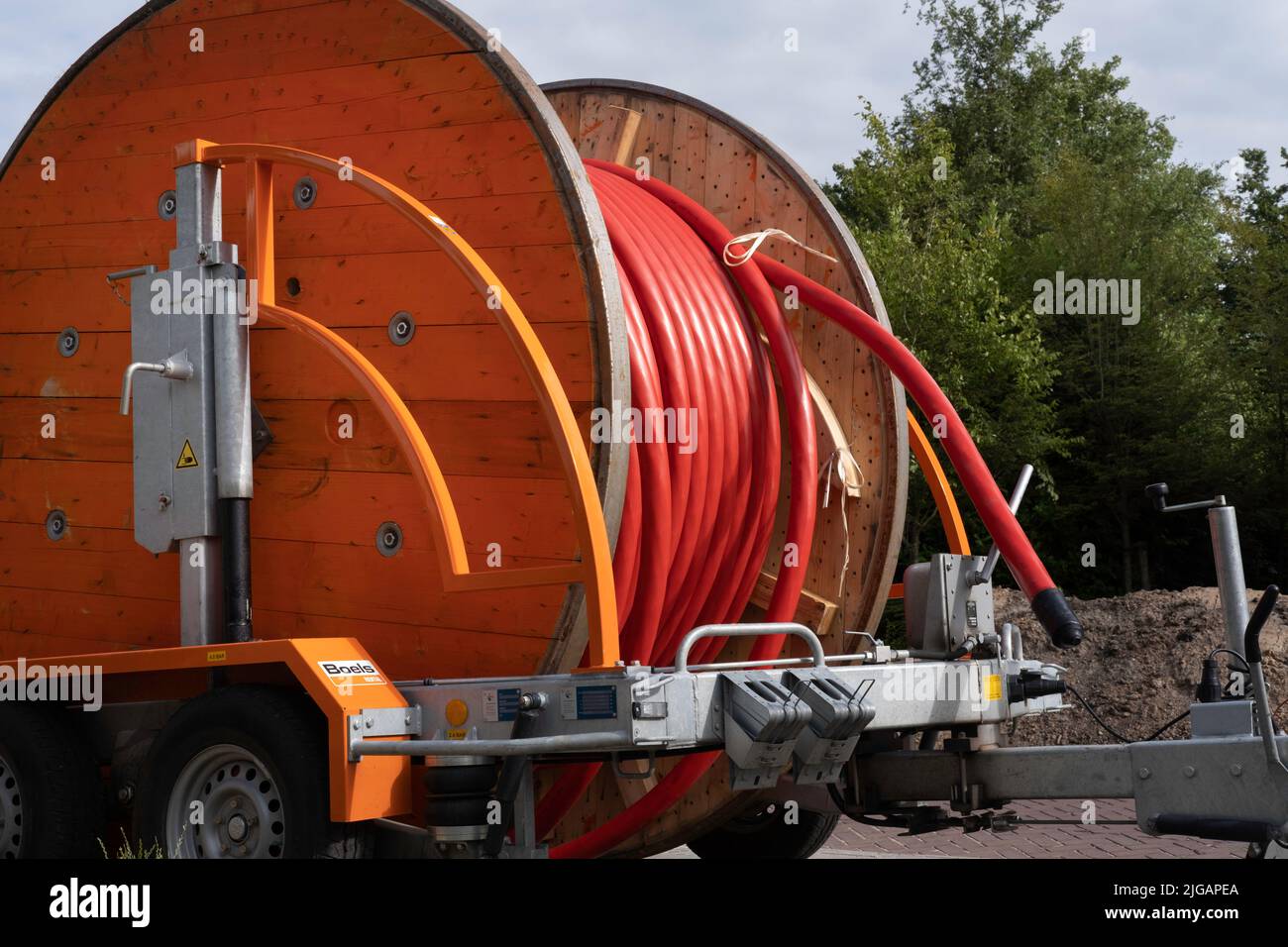 Large orange wooden spool for cable reel with red coiled electricity ...