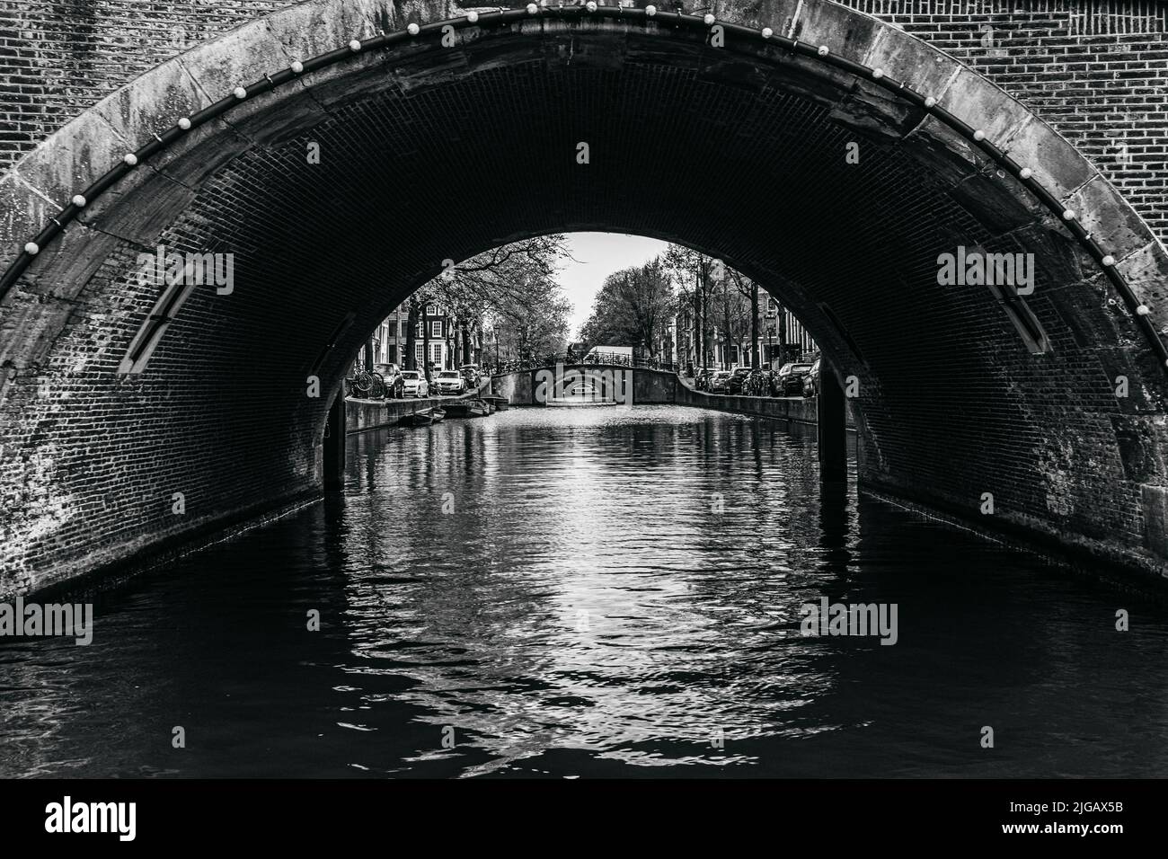 A flowing river under stony arch surrounded by growing trees in ...