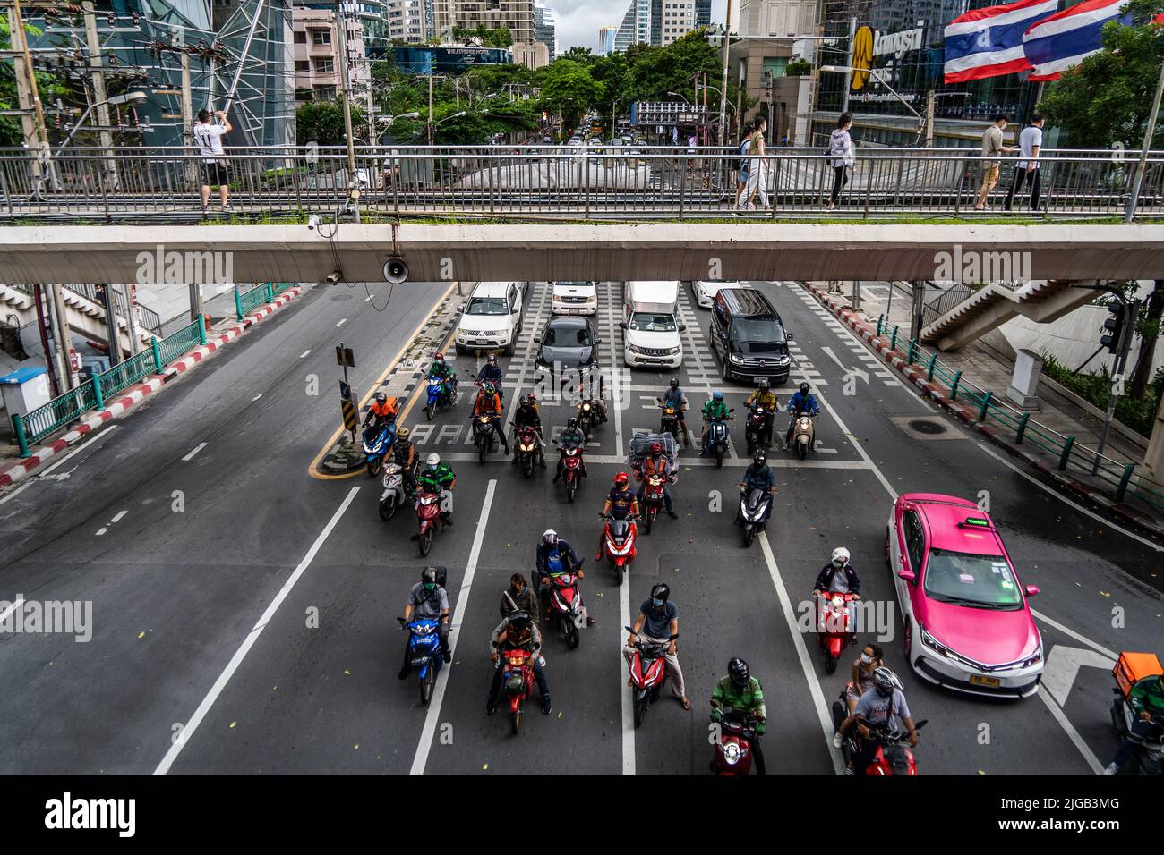 People walk on a pedestrian bridge over car traffic and motorcycles at ...