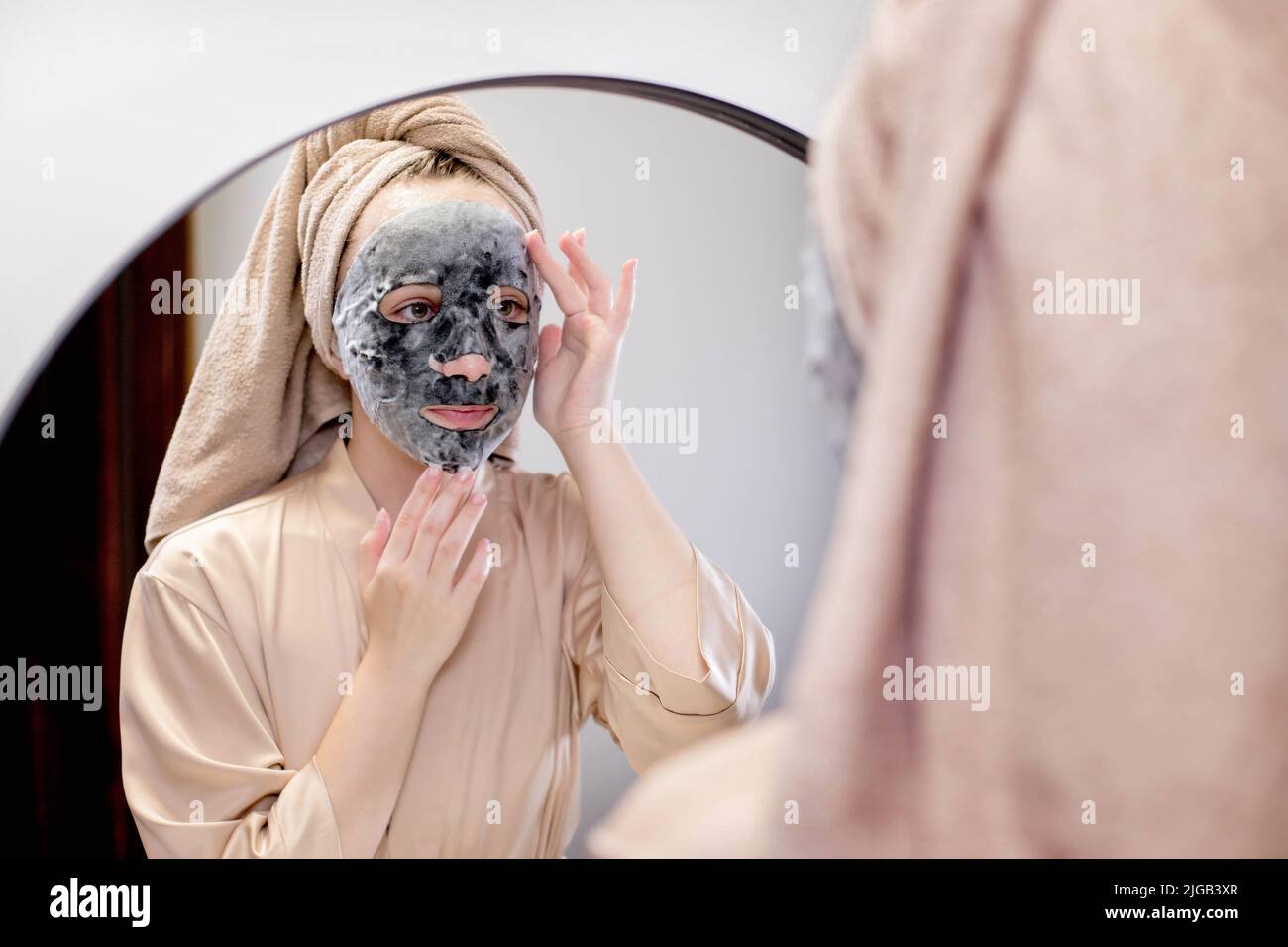 Young woman applying face mask in bathroom and smiling. Beautiful woman ...