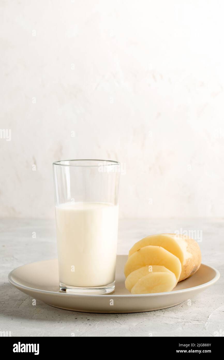 Vegan potato milk in glass with cut potato purified tuber on beige ...