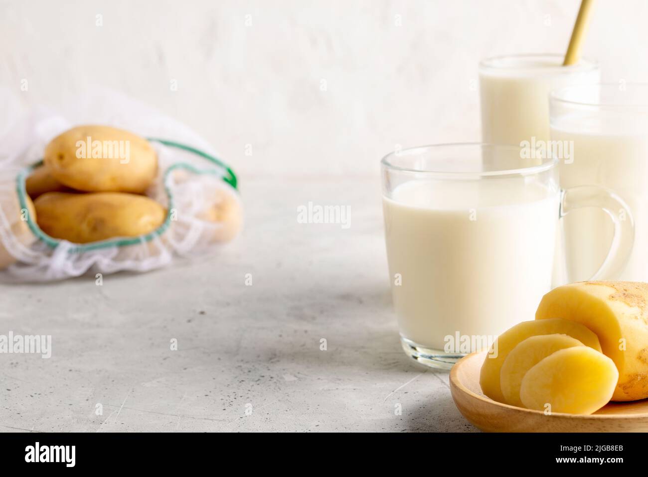 Vegetable vegan potato milk in glasses and potato tubers on concrete ...