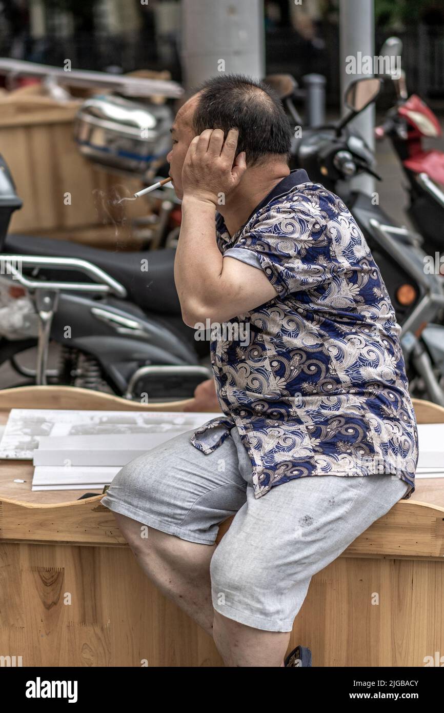 A vertical shot of a mechanic smoking a cigarette outside of his shop ...