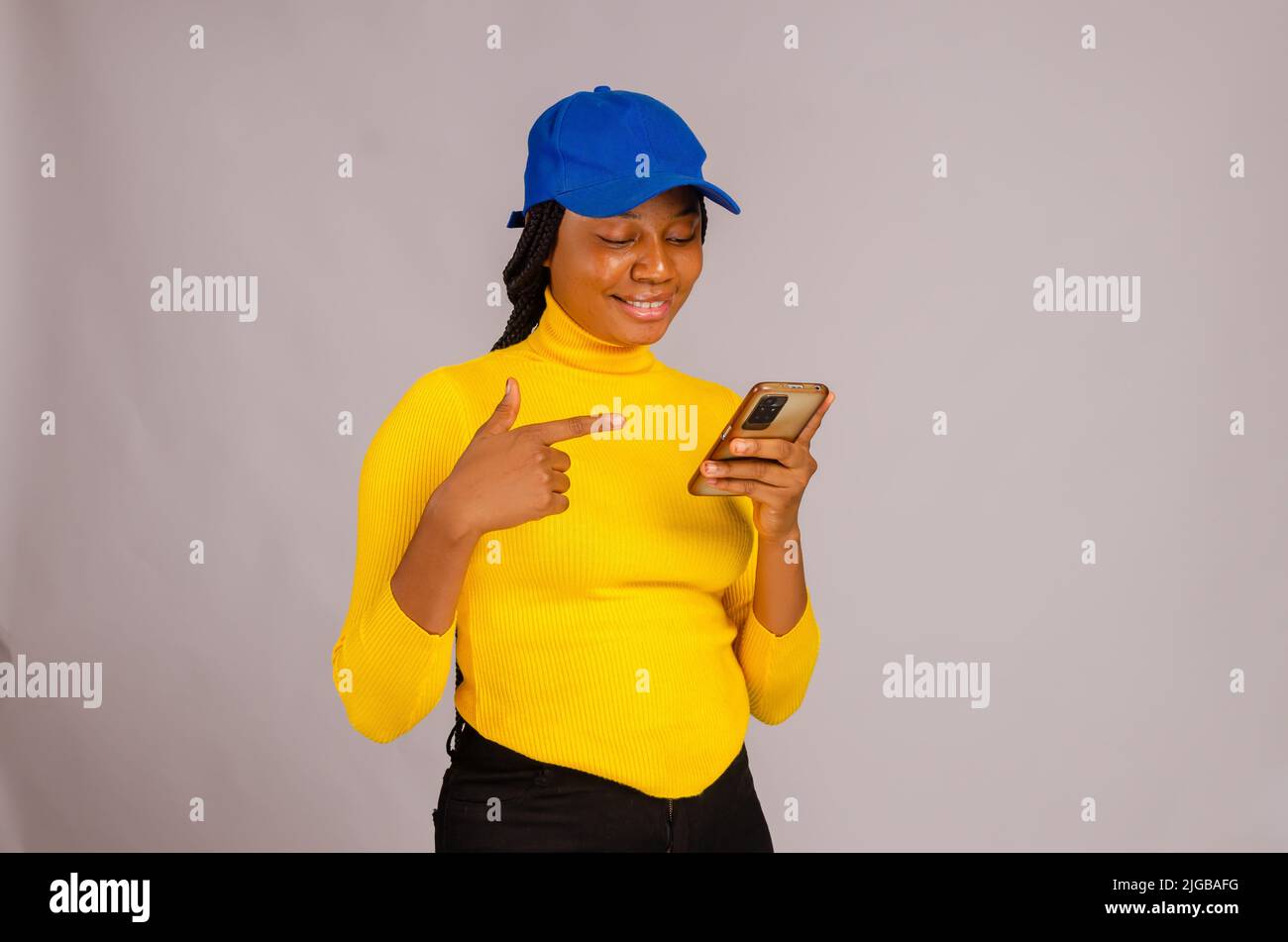 An African female model pointing at her smartphone in isolated white ...