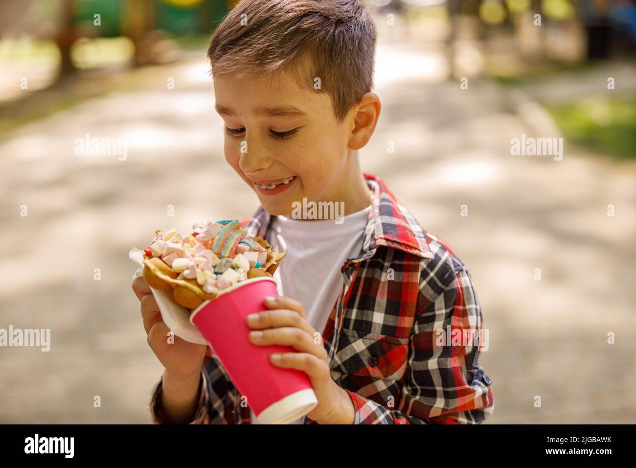 Portrait of cheerful cute little boy eating waffle with marshmallows at ...