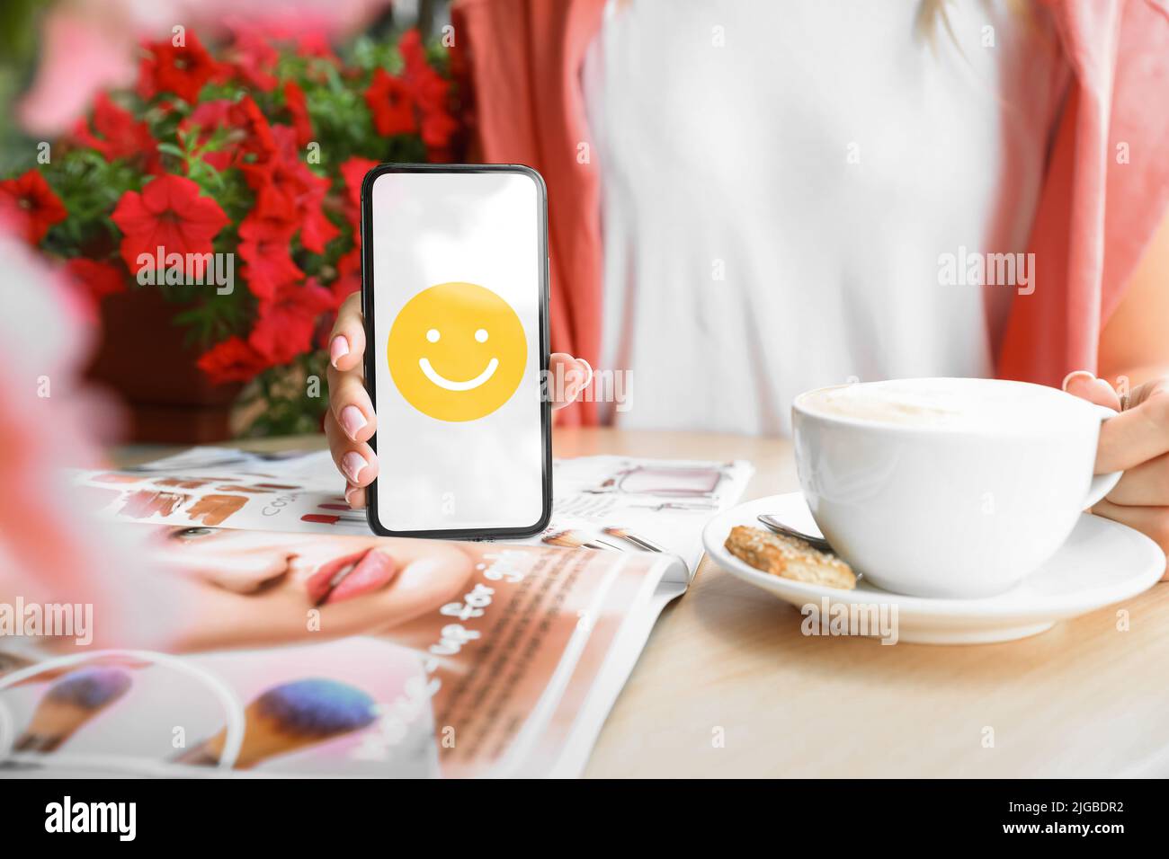 Woman holding phone with happy emoticon on screen in cafe, closeup ...
