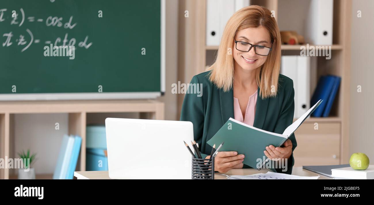 Beautiful female teacher at table in classroom Stock Photo - Alamy