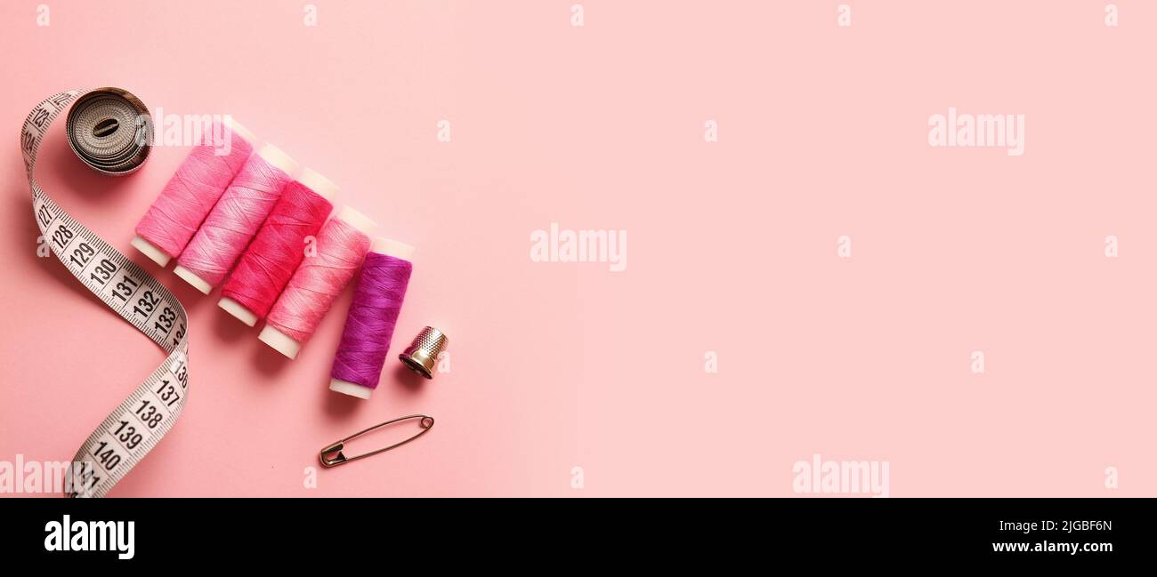 Colorful sewing threads and measuring tape on pink background with ...