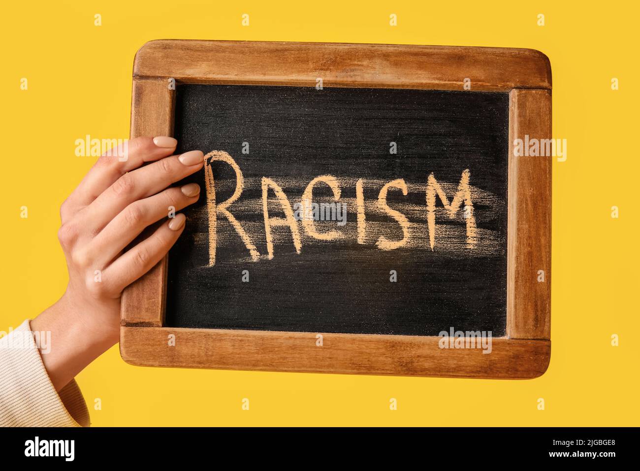 Human hand holding chalkboard with written word RACISM on color ...