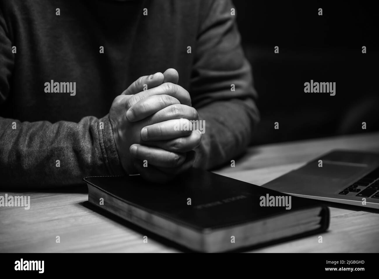 Praying mature man with Holy Bible sitting at table, black and white ...