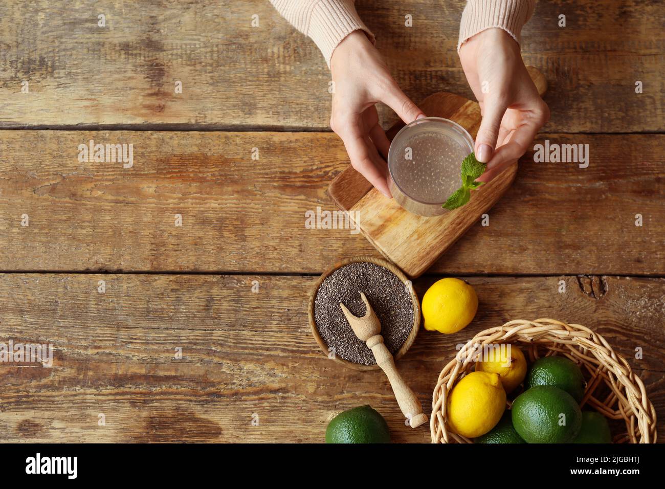 Woman adding mint leaves to glass of drink with chia seeds on wooden ...