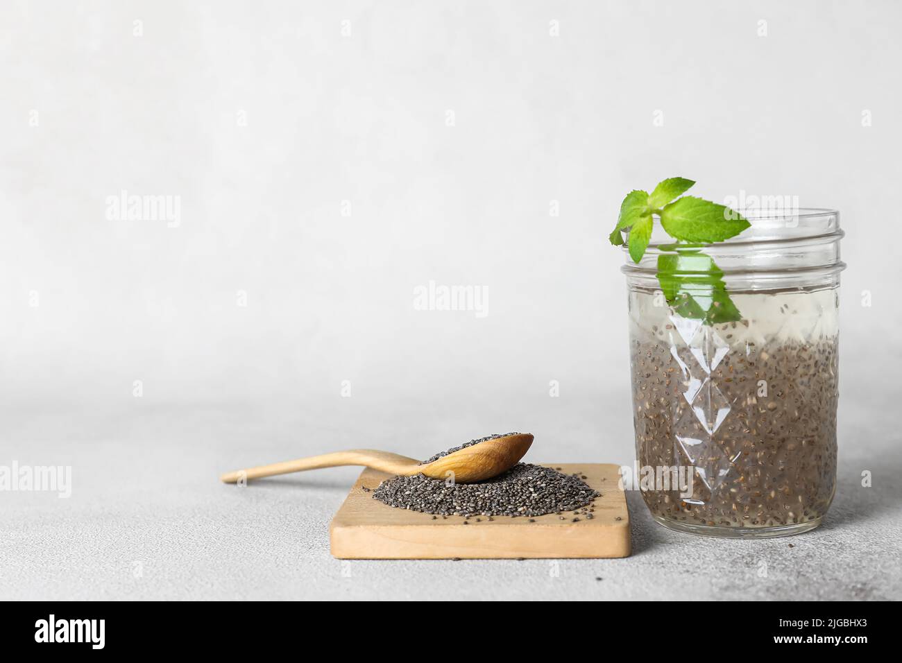 Glass of water with chia seeds, board and spoon on light background ...
