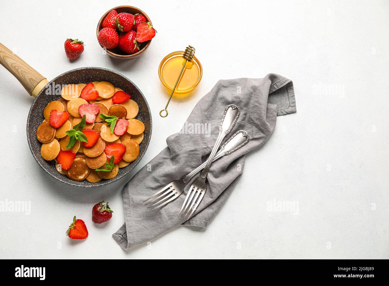 Frying pan with mini pancakes, strawberry and bowl with honey on white ...