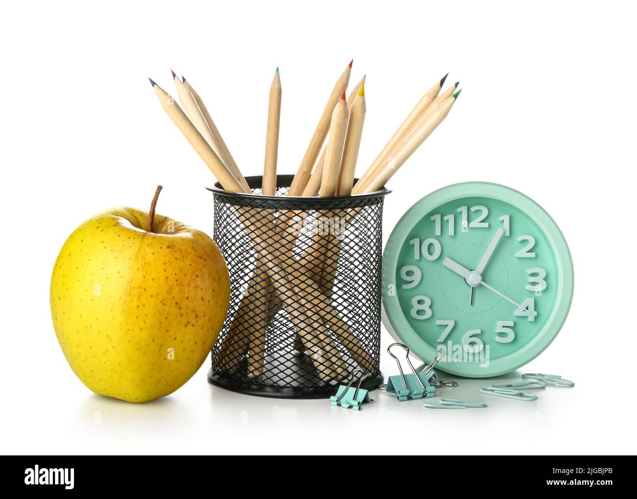 Holder with pencils, paper clips, alarm clock and apple on white ...
