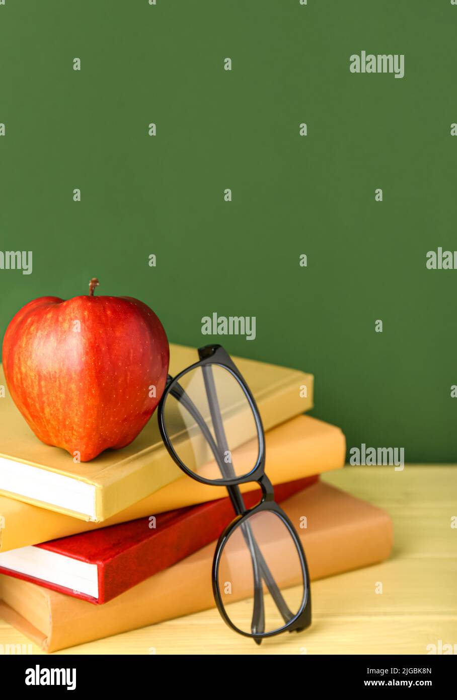 School books with apple and eyeglasses on table against green ...