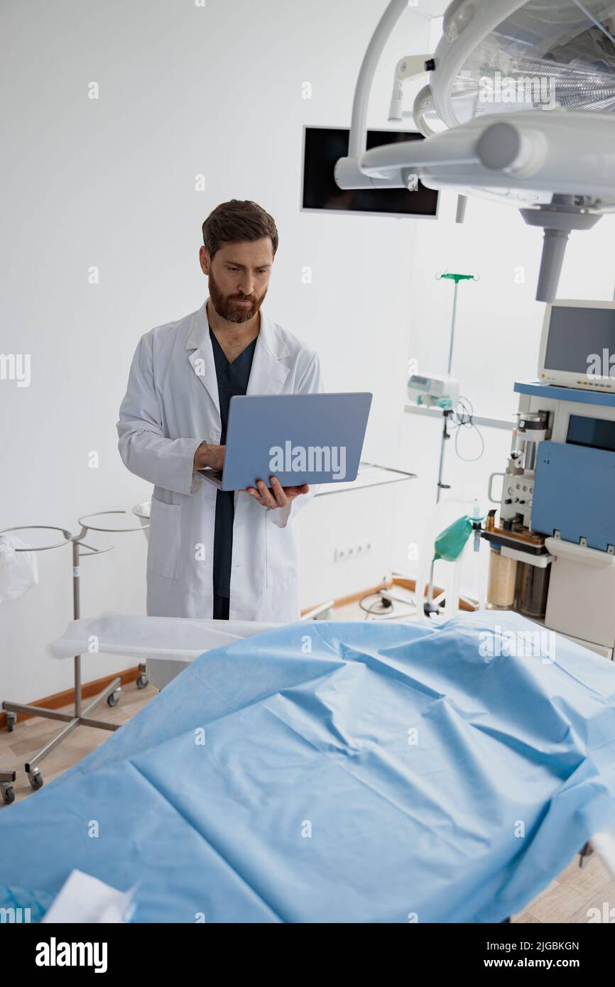 Professional doctor standing with laptop before operation in modern ...