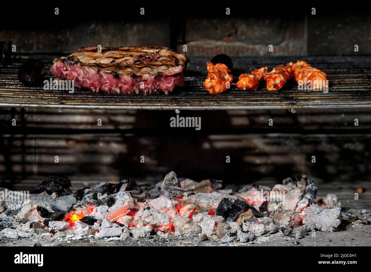 Pork ribs and marinated chicken skewers cooking over charcoal on a ...