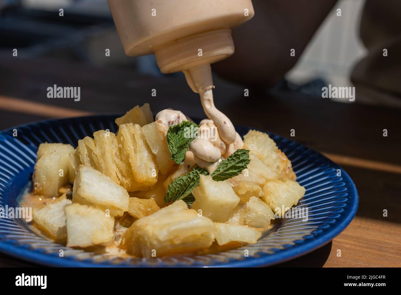 Fried yucca with mint leaves on a blue plate with homemade sauce ...