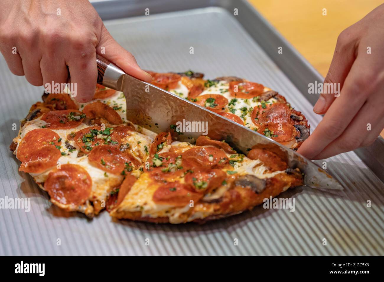A hand slicing a homemade pepperoni pizza with a Knife Stock Photo - Alamy