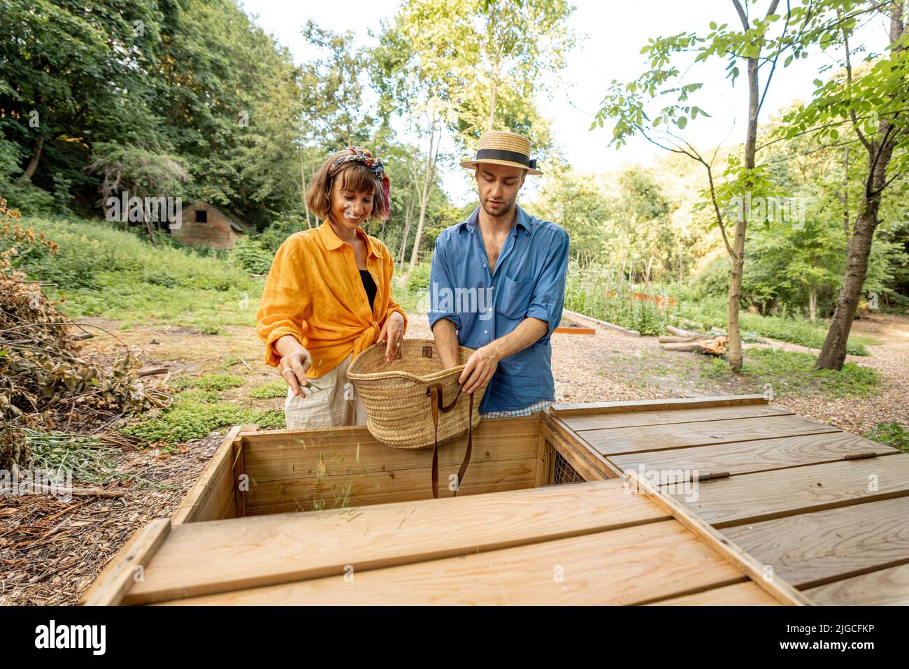 Couple throwing cut grass to compost wooden bin Stock Photo - Alamy