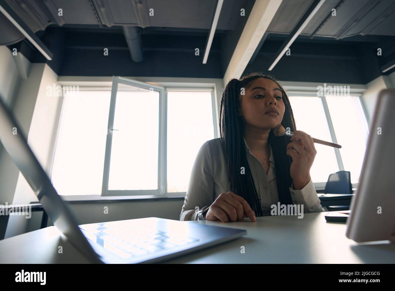 Female office worker looking in tabletop mirror during makeup ...