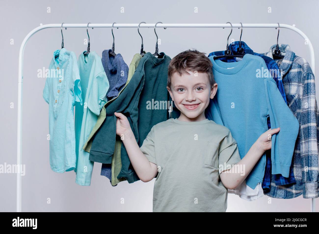 Boy preschooler standing by the hangers, racks up clothes, and chooses ...